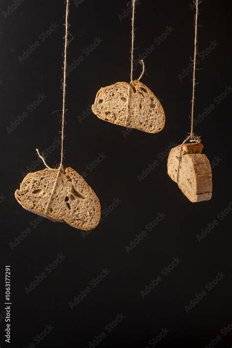 Slice Of Rustic Artisanal Bread Is Suspended Delicately By A Thin String Against A Black