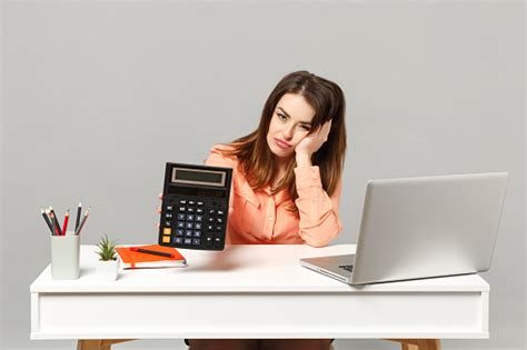 계산기를 들고 파스텔 캐주얼에 젊은 피곤 여자 앉아서 회색 배경에 고립 된 Pc 노트북과 흰색 책상에서 작동 합니다 성취 비즈니스 커리어 라이프 스타일 컨셉 복사 공간을