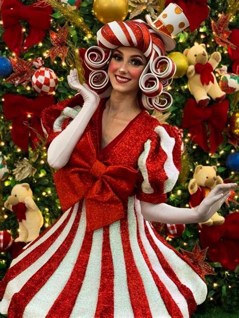 A Woman In A Red And White Dress Standing Next To A Christmas Tree With