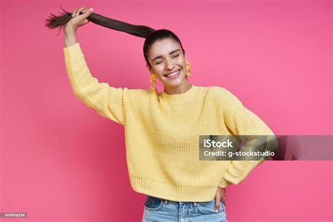 장난기 많은 젊은 여성이 긴 머리를 들고 색칠된 배경에 미소를 짓고 있습니다 한 명의 여자만에 대한 스톡 사진 및 기타 이미지