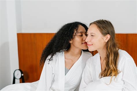 Dua Teman Remaja Putri Duduk Di Tempat Tidur Bersama Sementara Satu Mencium Pipi Temannya