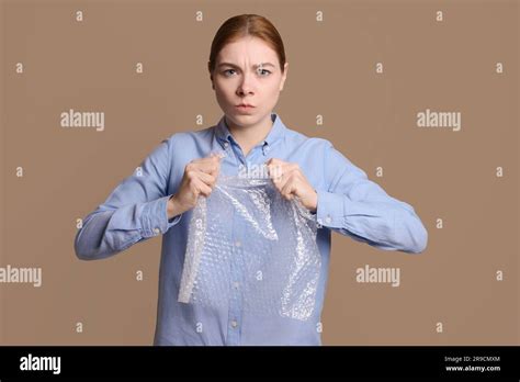 Angry Woman Popping Bubble Wrap On Beige Background Stress Relief
