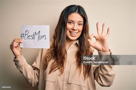 손가락으로 확인 기호를하고 어머니의 날을 축하하는 최고의 엄마 메시지와 종이를 들고 젊은 아름다운 여자 우수한 기호 갈색 머리에
