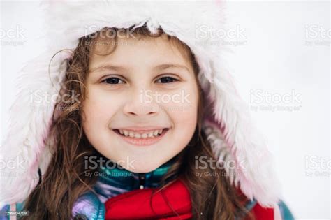 겨울 날에 야외에서 웃고 재미있는 귀여운 소녀 붉은 모자와 스카프에 긴 머리와 미소 예쁜 어린 소녀는 겨울 시간에 흰색 눈 덮인