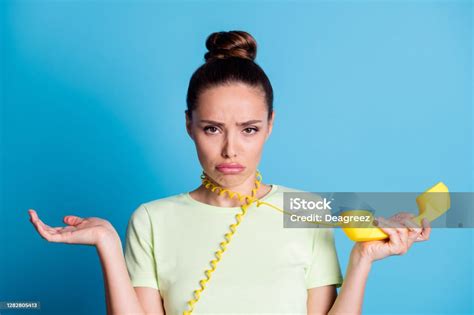 선명한 파란색 배경에 고립 된 목 주위에 와이어와 노란색 복고풍 전화를 유지 오해를 보여주는 슬픈 심술 소녀의 사진 초상화 T