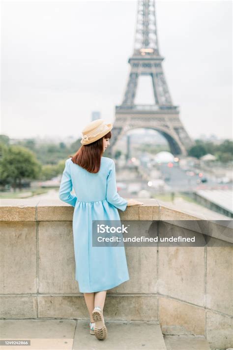 계단 근처를 걷는 예쁜 젊은 백인 소녀 배경에 에펠 탑 파리 매력적인 여자 에 블루 드레스 에 다시 유지 에 카메라 와 파리의