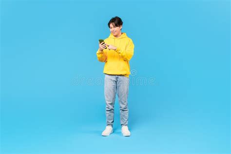 Asian Teen Guy Texting On Cellphone Standing On Blue Background Stock