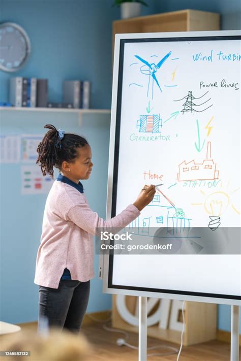 초등학교 과학 수업 귀여운 소녀는 인터랙티브 디지털 화이트보드를 사용하여 재생 가능 에너지가 어떻게 작동하는지 반 친구들로 가득 찬 교실에 보여줍니다 과학 수업 호기심 많은