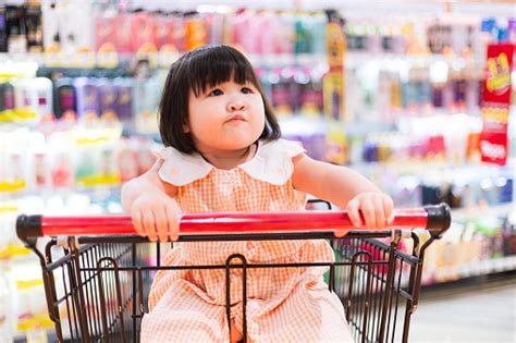 아시아 유아는 쇼핑몰의 쇼핑 카트에 앉아 있으며 12 세 아기의 초상화 이미지 슈퍼마켓에서 쇼핑하는 카트에 앉아 있는 행복한 아시아 어린이 소녀 18 23 개월에 대한 스톡