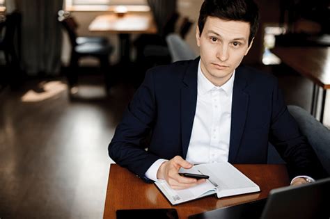 카메라를 진지하게 바라보며 스마트폰을 들고 점심을 기다리는 책상에 앉아 있는 자신감 있는 백인 사업가 검은색에 대한 스톡 사진 및 기타 이미지 Istock