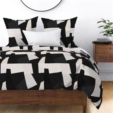A Bed With Black And White Comforter On Top Of It Next To A Plant