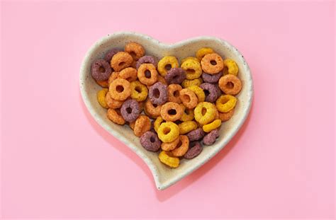 건조한 아이들의 아침 식사 여러 가지 색상의 반지를 분홍색 배경에 하트 형태로 세라믹 장식 접시에 담았습니다 건강한 생활방식에