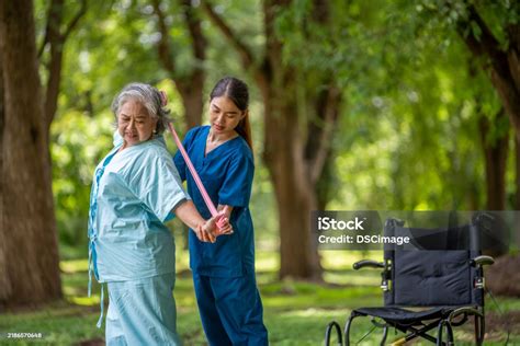 건강 관리 또는 물리 치료 간호사는 저항 밴드 간병인 개인 중심의 재활 노인 개념으로 스트레칭 또는 재활 운동을 수행하는 노인 여성을 돕고 있습니다 2명에 대한 스톡 사진