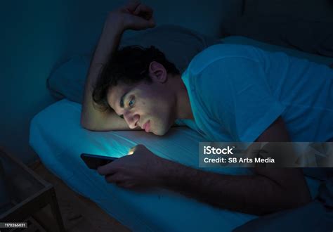 침대에서 늦은 밤에 스마트 폰으로 인터넷에서 채팅하고 서핑하는 중독 된 남자 지루한 불면증과 무디 빛 어두운 방에서 피곤 불면증과 모바일 중독 개념에서 누워있기에 대한 스톡