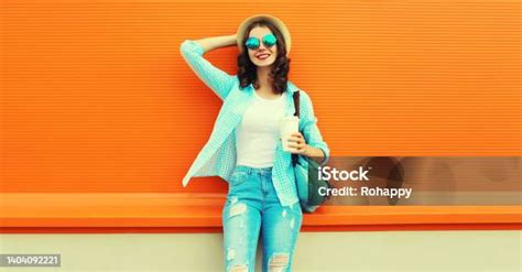 오렌지색 배경에 여름 밀짚모자와 배낭을 쓰고 커피 컵을 들고 행복한 미소 짓는 젊은 여성의 초상화 광고 텍스트를위한 빈 복사 공간 20 29세에 대한 스톡 사진 및 기타