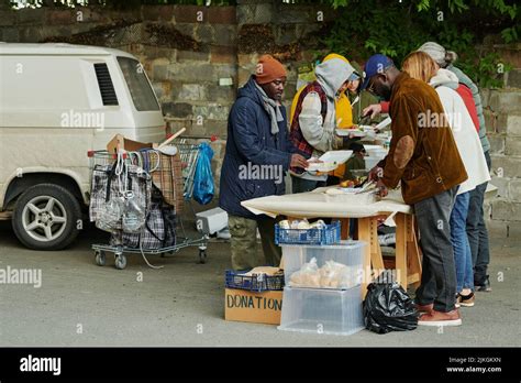Group Of Homeless People Getting Free Food From Volunteers During