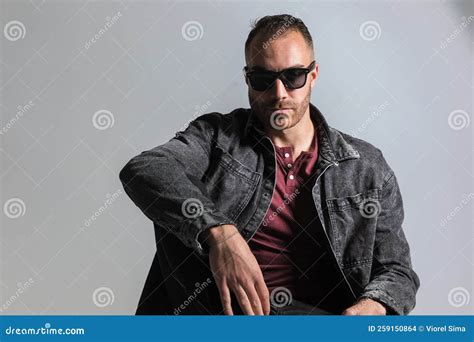 Joven Sentado Con Gafas De Sol Sosteniendo El Codo Sobre La Rodilla Y