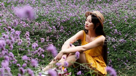 노란색 드레스와 밀짚 모자에 아름다운 여자는 보라색 Verbena 보나리엔시스 꽃 필드에 앉아 검은 긴 머리와 매력적인 중국