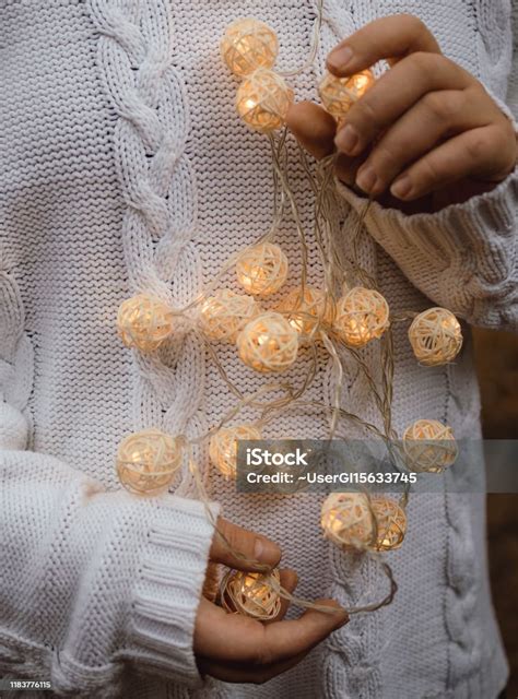 손바닥에 불이 들어오게 됩니다 여성의 손은 고리버들 둥근 공화환을 들고 있다 그녀의 손에 크리스마스 조명 따뜻한 새해 분위기 부드러운 초점흰색 스웨터에 소녀 12월에 대한