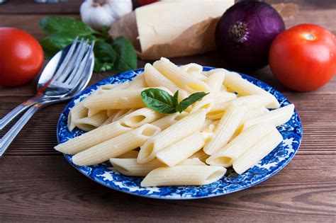 버터 치즈와 신선한 야채 재료 배경에 펜 네 파스타 요리 토마토 마늘 양파 포크와 스푼 바 질 나무 테이블에 빈티지 아름 다운 블루 플레이트입니다 격리 그릇에 대한 스톡