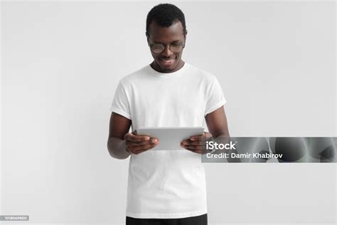가로 사진의 잘생긴 아프리카 남성 서 안경을 착용 하 고 그가 잡고 태블릿 컴퓨터를 사용 하 여 회색 배경에 고립 콘텐츠 만족