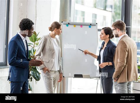 Four Multiethnic Colleagues In Formal Wear Standing Near Flipchart In