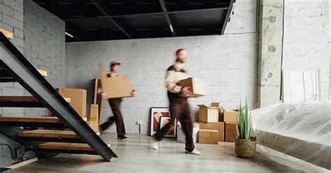 포장된 판지 상자를 들고 새 아파트 집 또는 스튜디오로 패키지를 배달하는 것을 돕는 두 명의 젊은 로더의 흐릿한 움직임 사진