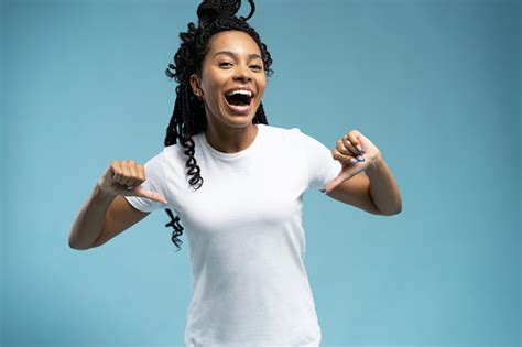 흰색 티셔츠를 입고 파란색 배경에 고립 된 티셔츠에 손가락을 가리키는 웃는 아프리카 계 미국인 여성 20 24세에 대한 스톡 사진 및 기타 이미지 Istock