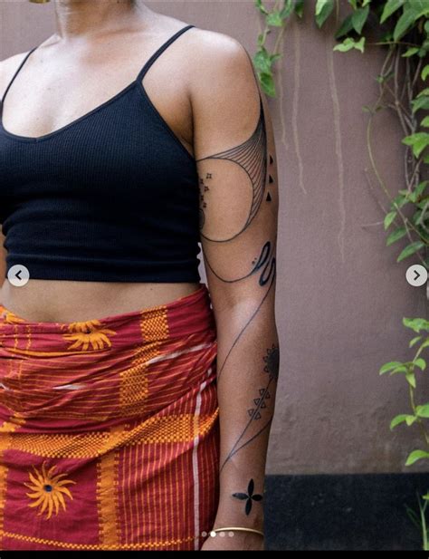 A Woman With Tattoos Standing In Front Of A Wall Wearing A Red And