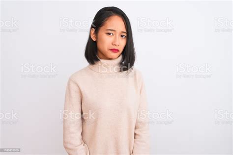 고립된 흰색 배경 위에 서있는 터틀넥 스웨터를 입은 젊은 중국 여성은 우울하고 고민에 대해 걱정하고 화가 나서 두려워합니다 슬픈 표정 갈색 머리에 대한 스톡 사진 및 기타