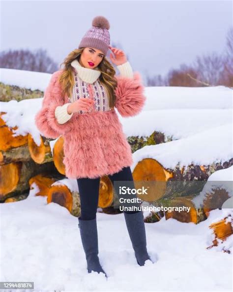 금발의 소녀는 분홍색 모피 재킷과 눈 속에서 보라색 모자를 쓰고 포즈를 취하고 있습니다 얼음으로 자른 나무 옆에 겨울 라이프 스타일 12월에 대한 스톡 사진 및 기타 이미지