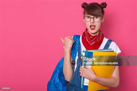 즐거운 머리 만두를 가지고 노란색 폴더를 들고 흰색 티셔츠 데님 바지 빨간 반다나 안경 어깨에 파란색 배낭을 들고 즐거운 Apearance와 여자의 수평 샷 T 셔츠에 대한