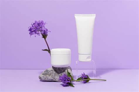 흰색 모형 튜브와 보라색 고립된 배경에 꽃과 돌이 있는 크림 병 얼굴과 몸 피부를 위한 천연 화장품의 개념 0명에 대한 스톡