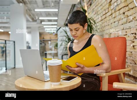 Young Businesswoman Sitting Near Table With Gadgets Looking At Folder