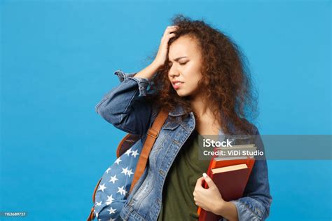 데님 옷에 젊은 슬픈 아프리카계 미국인 소녀 사춘기 학생 배낭은 파란색 배경 스튜디오 초상화에 고립 된 책을 보유 고등학교 대학