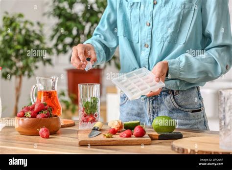 Woman Putting Ice Cubes Into Glass For Strawberry Lemonade In Kitchen