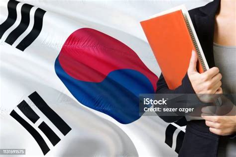 한국 언어의 개념을 배운다 백그라운드에서 대한민국 국기와 함께 서 있는 젊은 여자 책을 들고 교사 오렌지 빈 책 표지 대학교에
