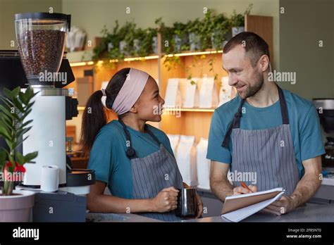 Waist Up Portrait Of Two Young Baristas Smiling While Enjoying Work In