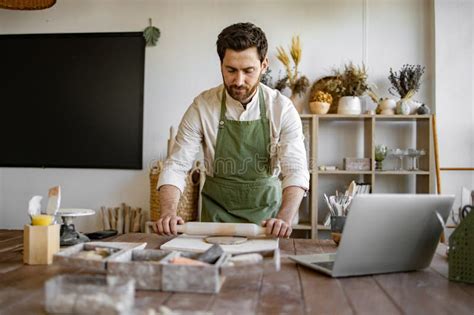 mature male potter flattens clay with rolling pin to create handmade