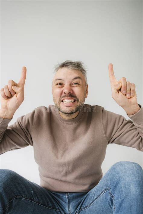 A Playful Portrait Of A Man Sitting Pointing Upwards With Both Hands His Joyful Expression And