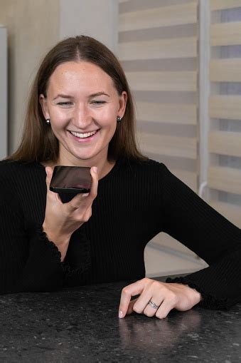 부엌 식탁에 앉아 스마트 폰으로 오디오 메시지를 녹음하고 음성 통신을위한 모바일 앱을 사용하여 웃고 대화를 즐기는 젊은 여성 세로 사진 20 24세에 대한 스톡 사진 및