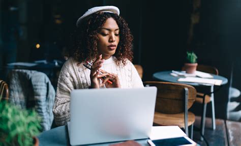 카페 테라스에 앉아 프로젝트 계획을 위한 연구를 하는 창의적인 어두운 피부의 여성 디자이너 온라인 학습 과정 및 메일 확인을 위해 노트북 컴퓨터를 사용하는 아름다운 잠겨