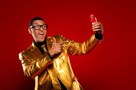 황금색 양복을 입은 스타일리시한 남자가 생동감 넘치는 배경을 배경으로 빨간 휴대전화를 들고 포즈를 취하며 기쁨과 카리스마를 표현합니다 30 34세에 대한 스톡 사진 및 기타