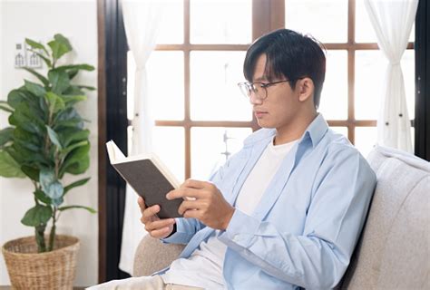 종이책이나 일기를 들고 안경을 쓴 젊은 아시아 남성의 초상화 거실의 집 소파에 앉아 문학을 읽거나 근무 일정 계획을 확인하는