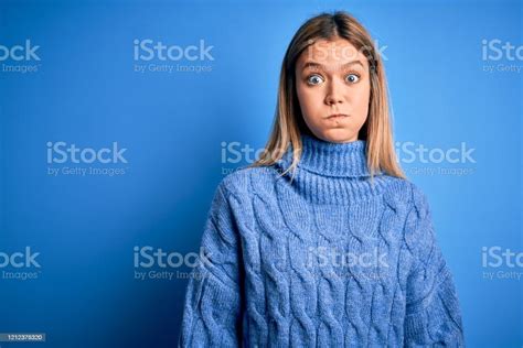 젊은 아름 다운 금발 여자 겨울 울 스웨터를 입고 블루 고립 된 배경 퍼핑 뺨 재미 있는 얼굴 공기 미친 표정으로 입이 팽창 가득 찬에 대한 스톡 사진 및 기타 이미지