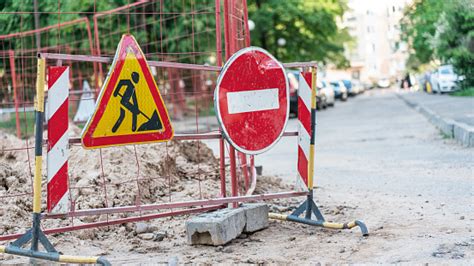 도시 거리의 건설 현장에는 진입 금지 표지판과 도로 공사를 묘사한 삼각형 경고 표지판이 있는 금속 바리케이드로 표시되어 있습니다 지역은 빨간 그물망으로 울타리가 쳐져