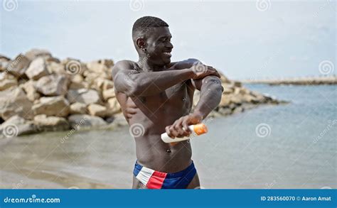 African American Man Tourist Standing Shirtless Applying Sunscreen At