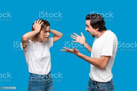 젊은 금발의 여성과 브루넷 수염 남자의 부부는 흰색 티셔츠와 파란색 배경 위에 고립 된 서 서 서 서 서 있는 흰색 티셔츠와