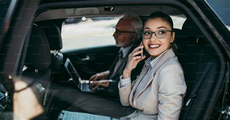 잘 생긴 고위 사업가와 그의 젊은 여성 동료 또는 동료가 고급 자동차의 뒷좌석에 앉아 있습니다 그들은 이야기하고 웃고 노트북과 스마트 폰을 사용합니다 기업 비즈니스