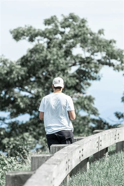 흰색 티셔츠와 파란색 데님 청바지를 입은 남자가 갈색 나무 위에 서 있는 흰색 모자를 쓰고 있다 사진 Unsplash의 무료